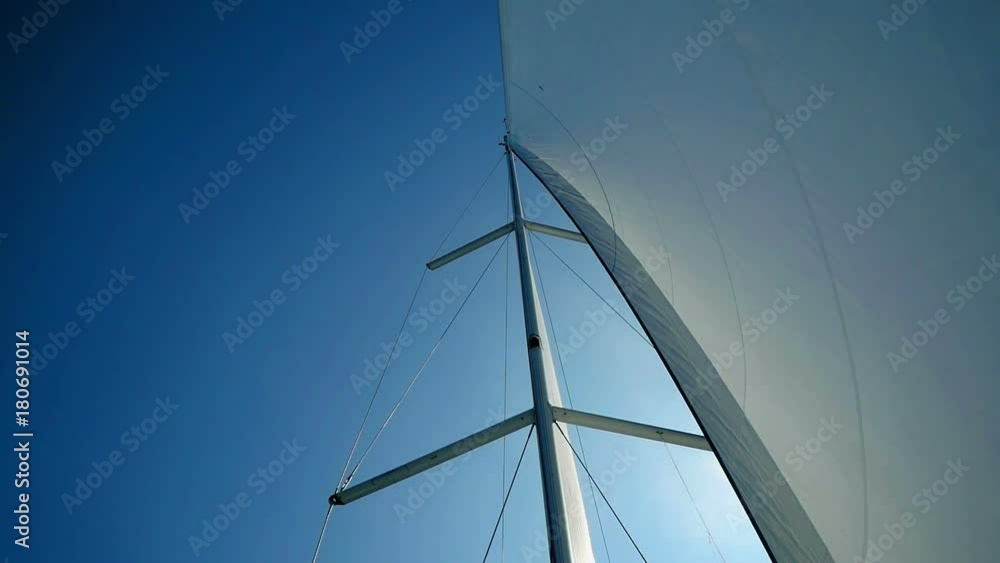 Sailing boat main mast with perfectly curved main sail and blue sky ...