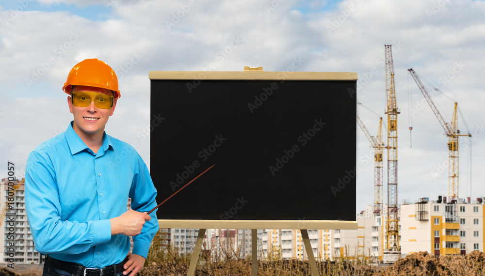 Happy smiling builder worker man in a hardhat holding in hands pointer ...