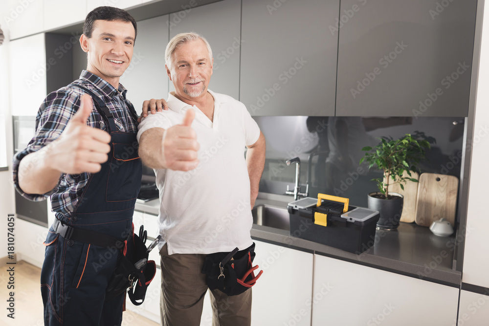 Two male plumbers posing in a modern kitchen. They have a special ...
