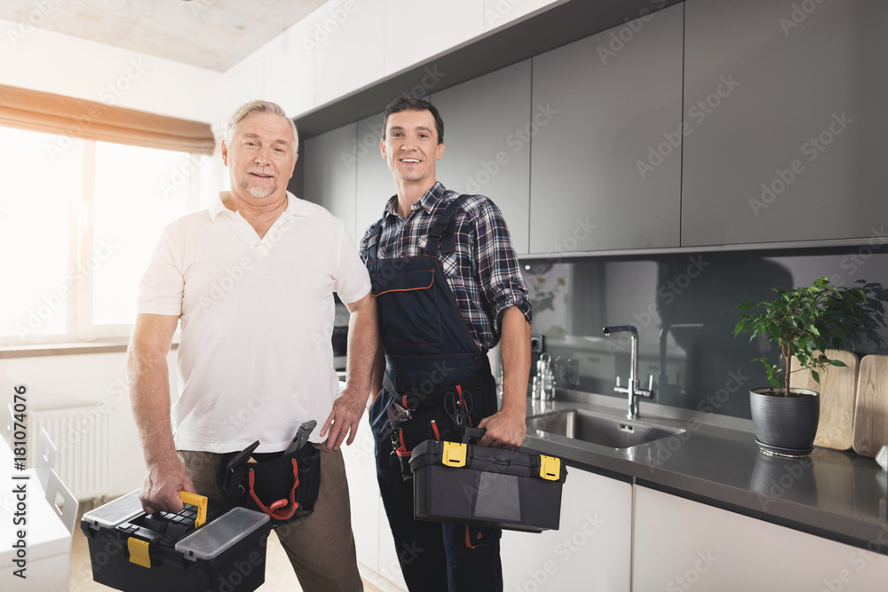 Two men of plumbers stand in the kitchen and pose with black toolboxes ...