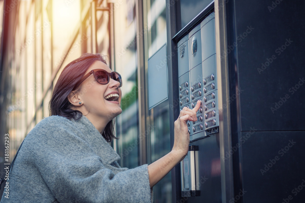 Happy woman using intercom at building entrance. Stock Photo | Adobe Stock