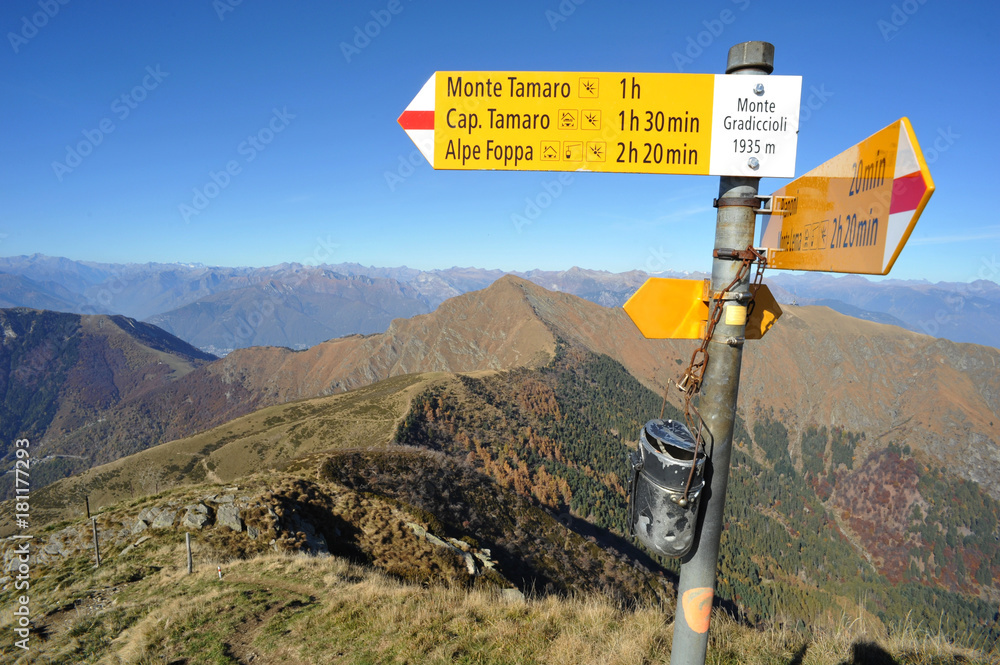 Wegweiser aus gelb beschichtem Aluminium an Wanderweg an den Berghängen ...