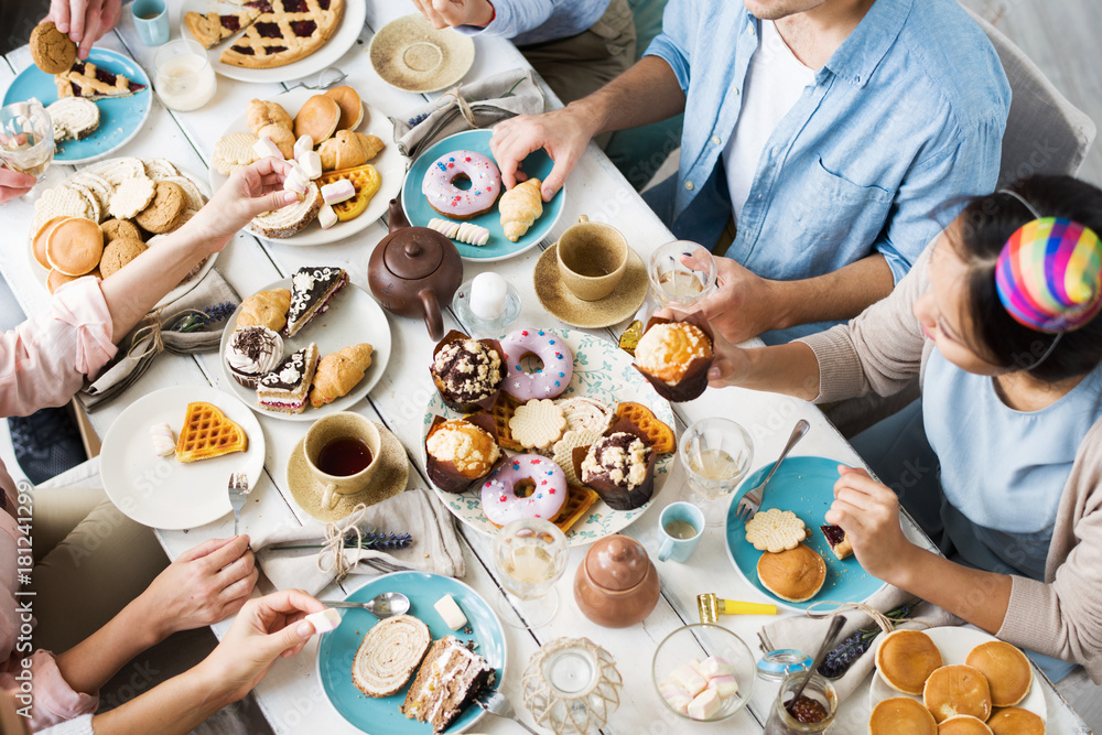 Served table with variety of sweet food and group of young people ...