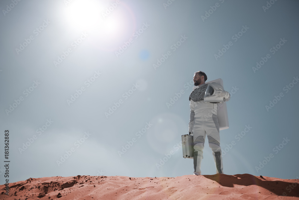 Confident spaceman is holding helmet and moving across wilderness. He ...