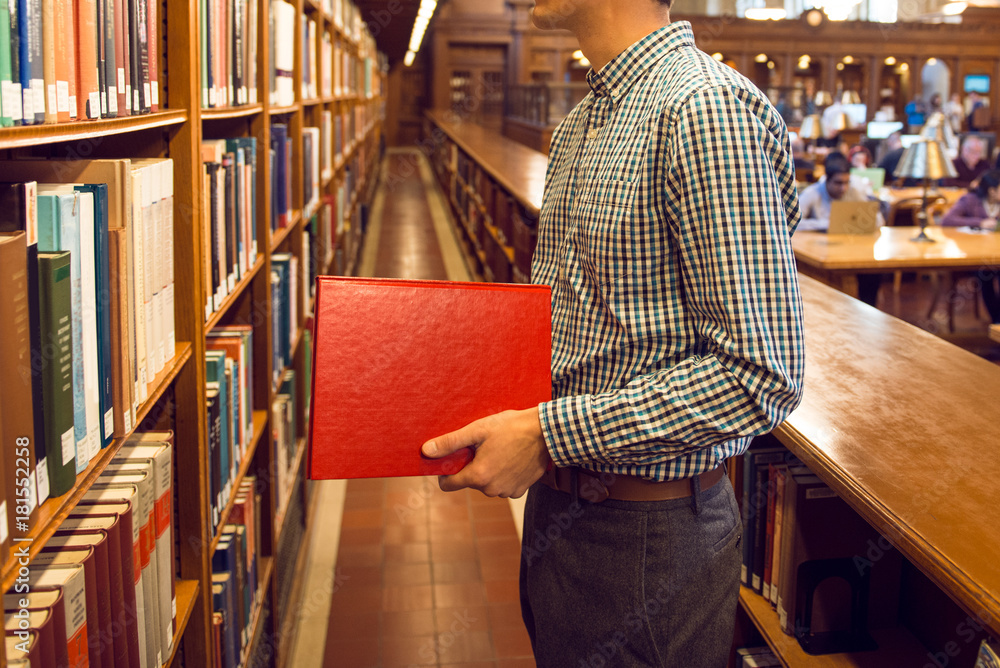 Student man taking the book from bookshelf in public library and going ...