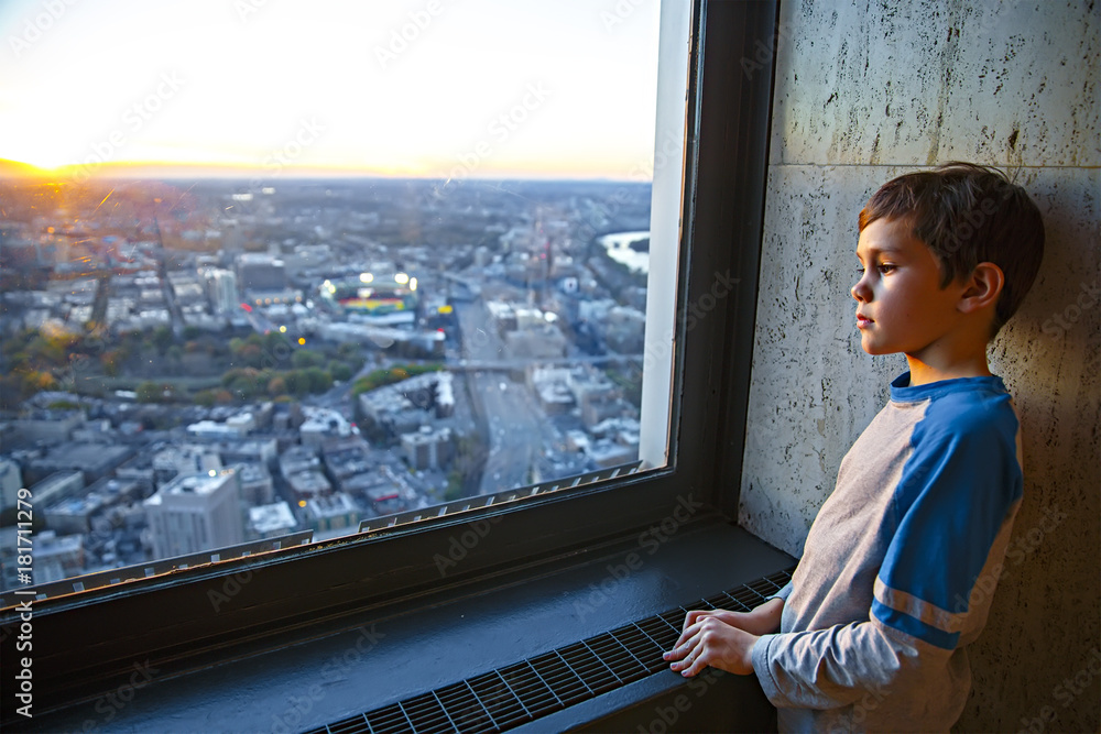thoughtful boy standing at the window. the child looks at the city from ...