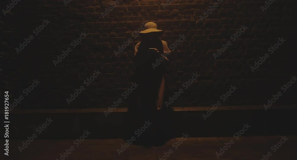 Stylish Caucasian female standing near brick wall at night, checking ...
