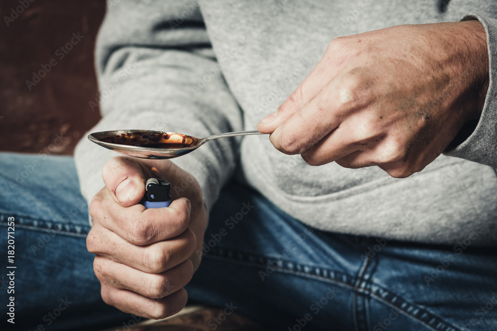 The hands of a drug addict melting cocaine in a spoon. A man holds a ...