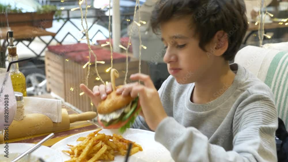 the boy is eating a hamburger in a cafe. 4k. a hamburger with a cutlet ...