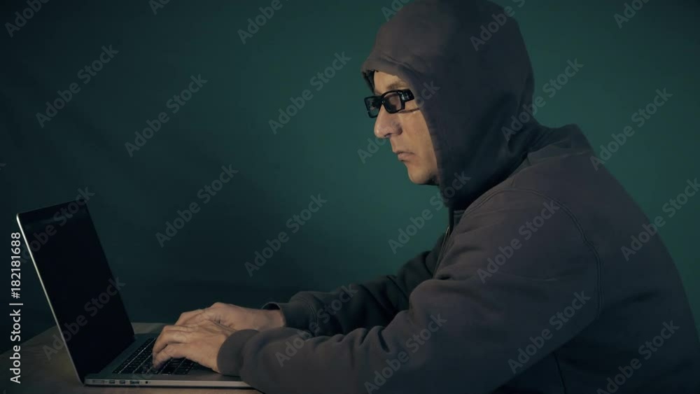 Hoody Man Coding. Profile side view of white man sitting at table and typing at laptop computer ...