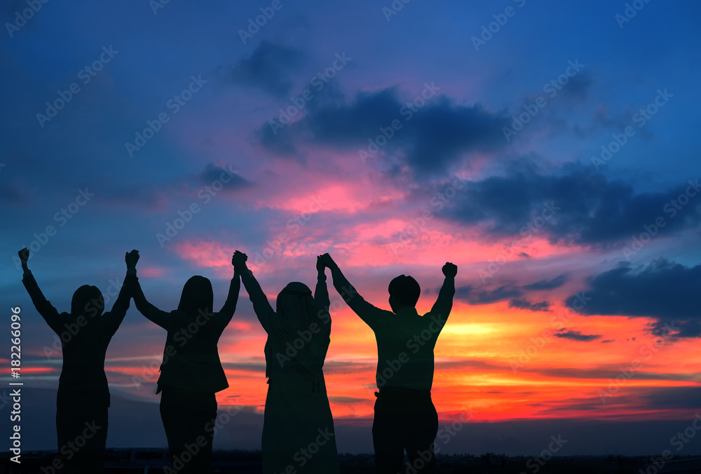 Silhouette of happy business team hold hands up in sunset sky ...