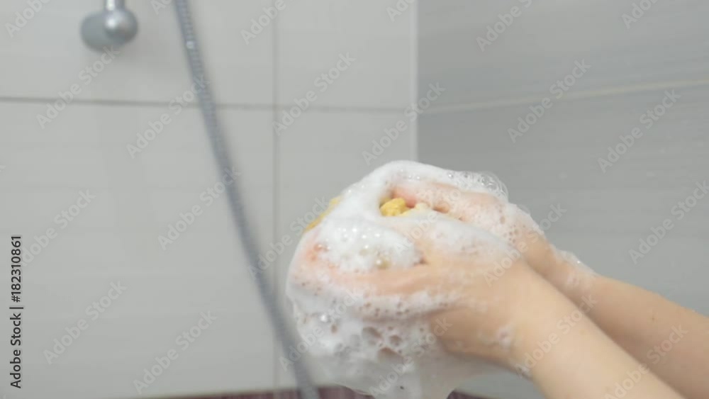 Woman's hand presses a bottle of liquid soap onto soft bath puff or ...