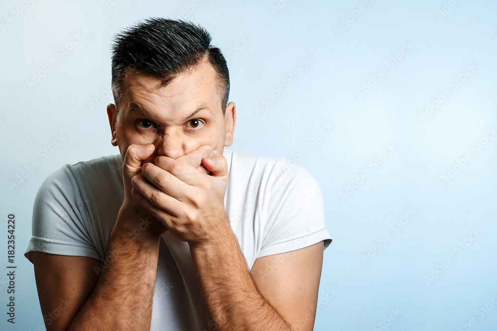 Portrait of a man on a light background, covers his mouth with his ...