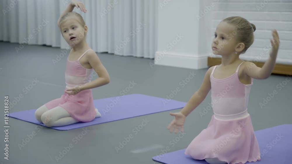 Two little girls sit on their laps and do dance exercises on training ...