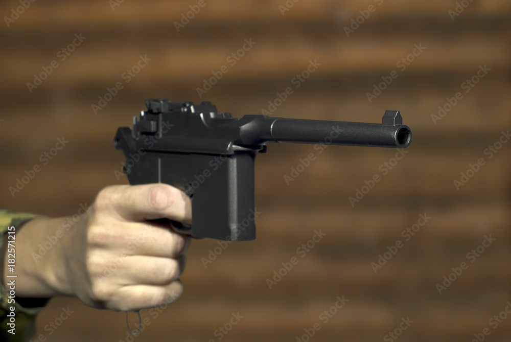 A man's hand with a vintage semi-automatic pistol points past the frame ...