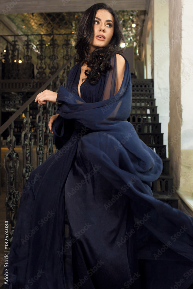 Beautiful young girl in blue dress, running looks back on the stairs ...