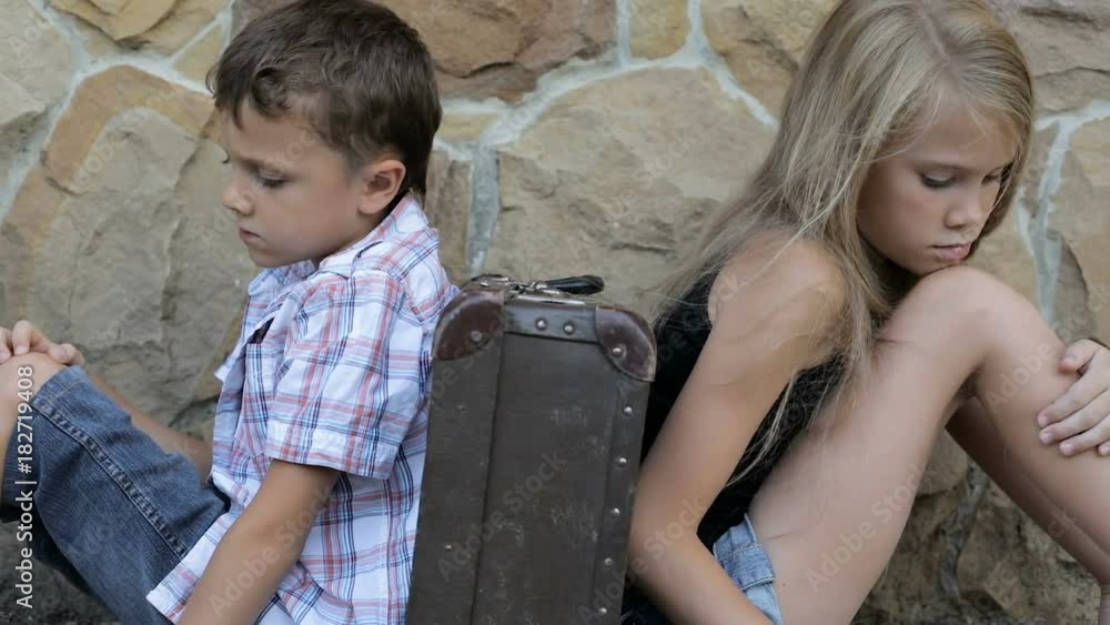 sad brother and sister are sitting by the wall with a suitcase Stock ...