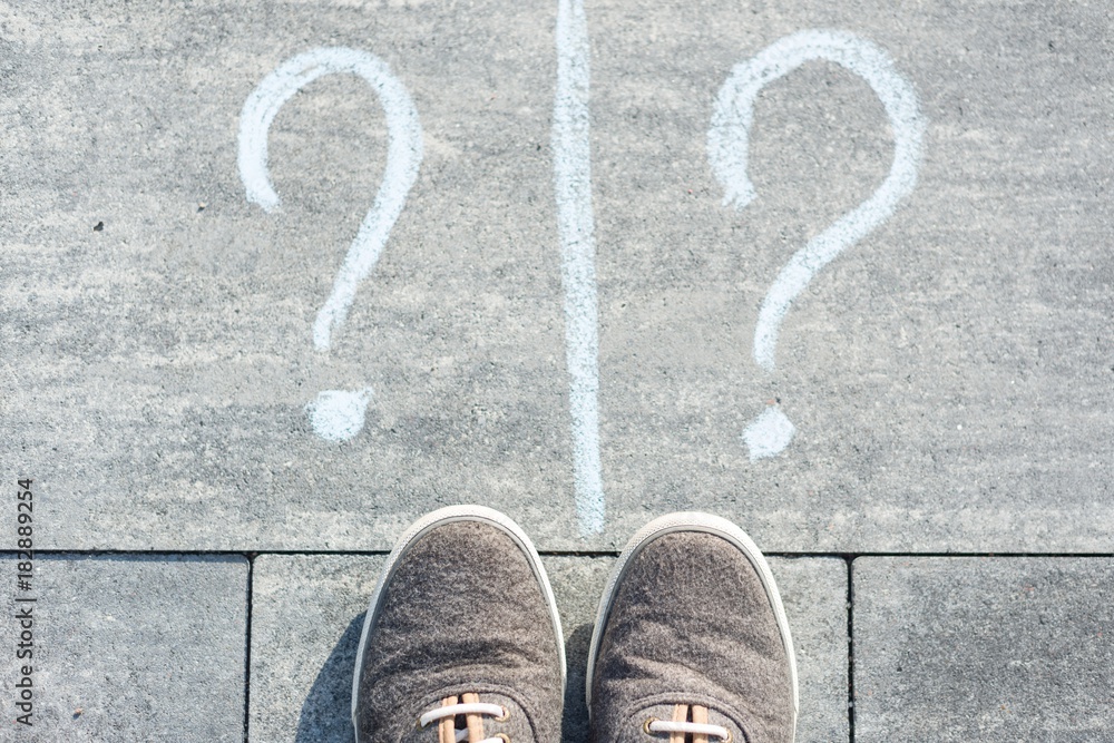 Two question marks are handwritten on an asphalt road with sneakers ...