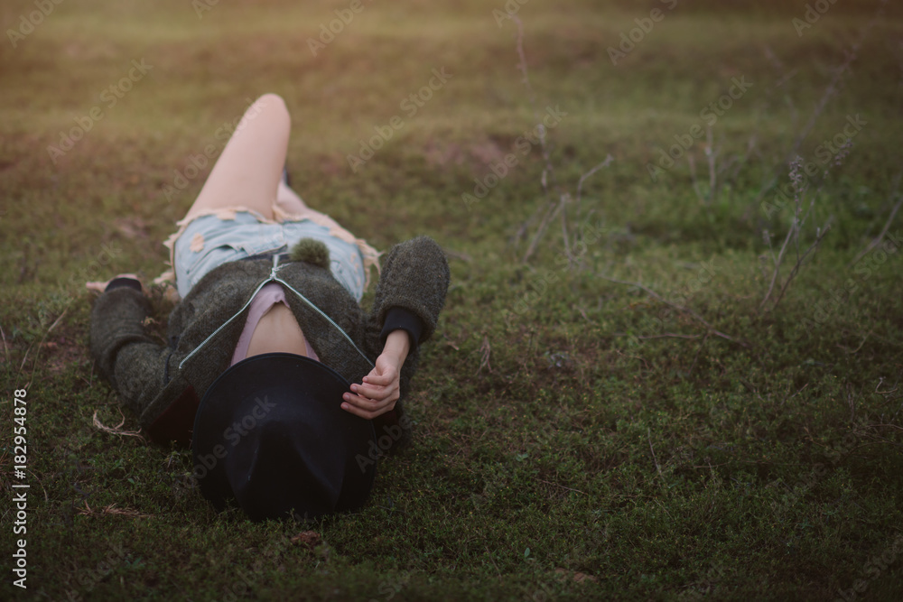 Portraif of woman lie supine on grass and wearing black hat close her ...