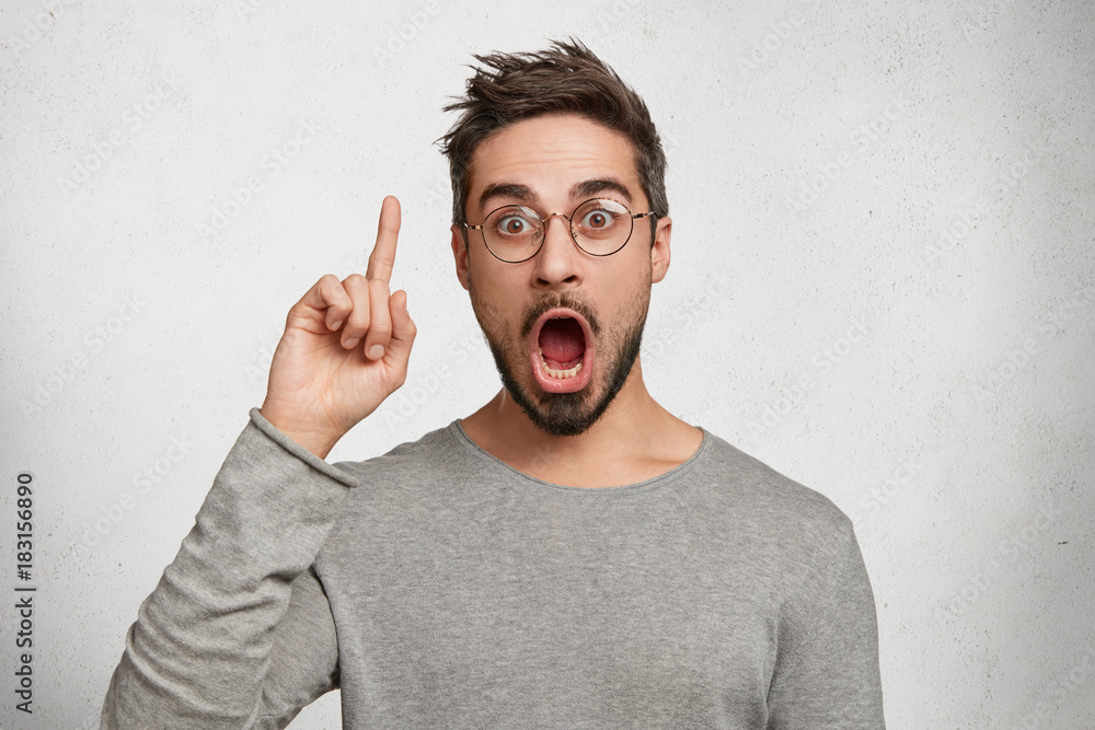 Amazed stupefied bearded handsome man opens mouth widely, raises fore ...