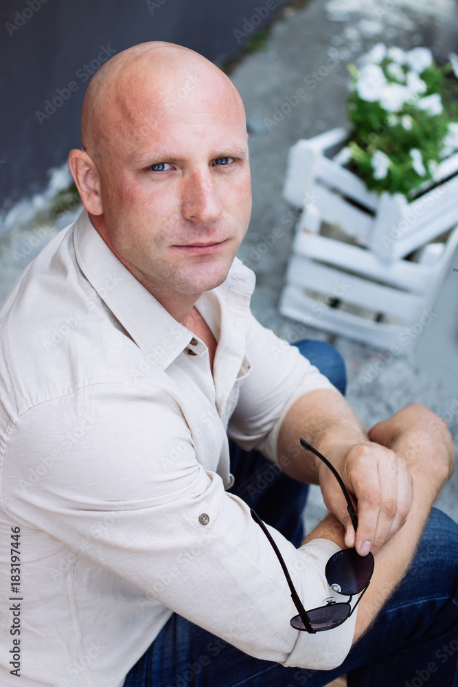 Bald handsome man sit on the flowers background, nature shirt, jeans ...