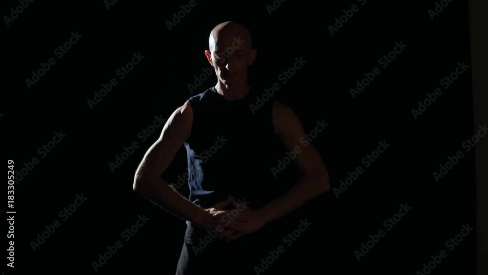 Half-lit silhouette of a man stretching in a darkened room with a ...