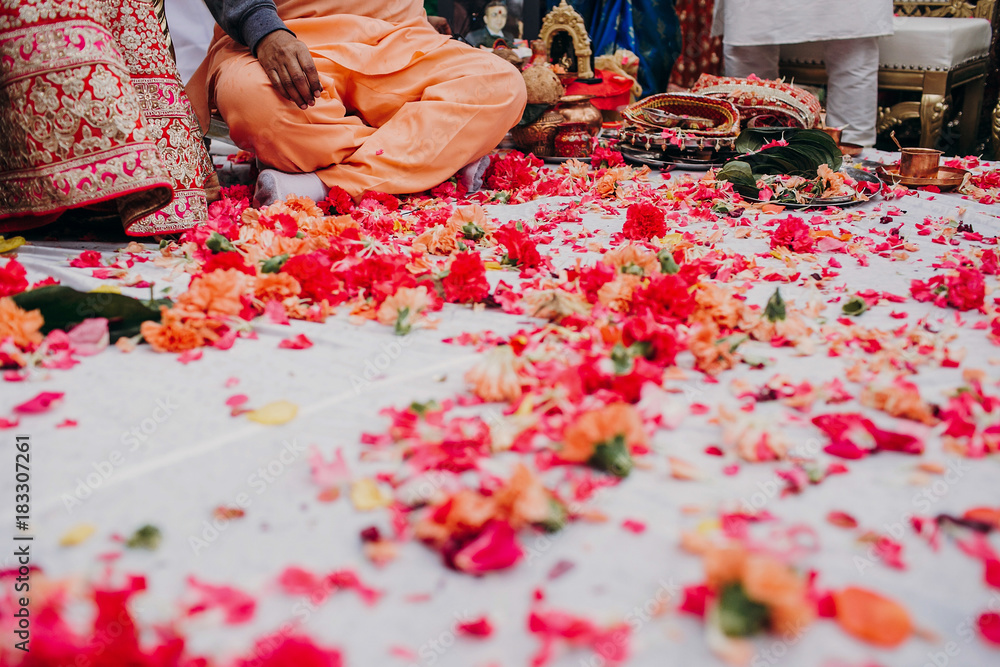 Pink and orange flowers lie before the feet of Indian wedding couple ...