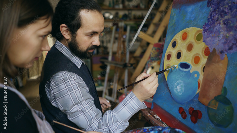 Skilled artist man teaching young girl to draw paintings and explaining ...