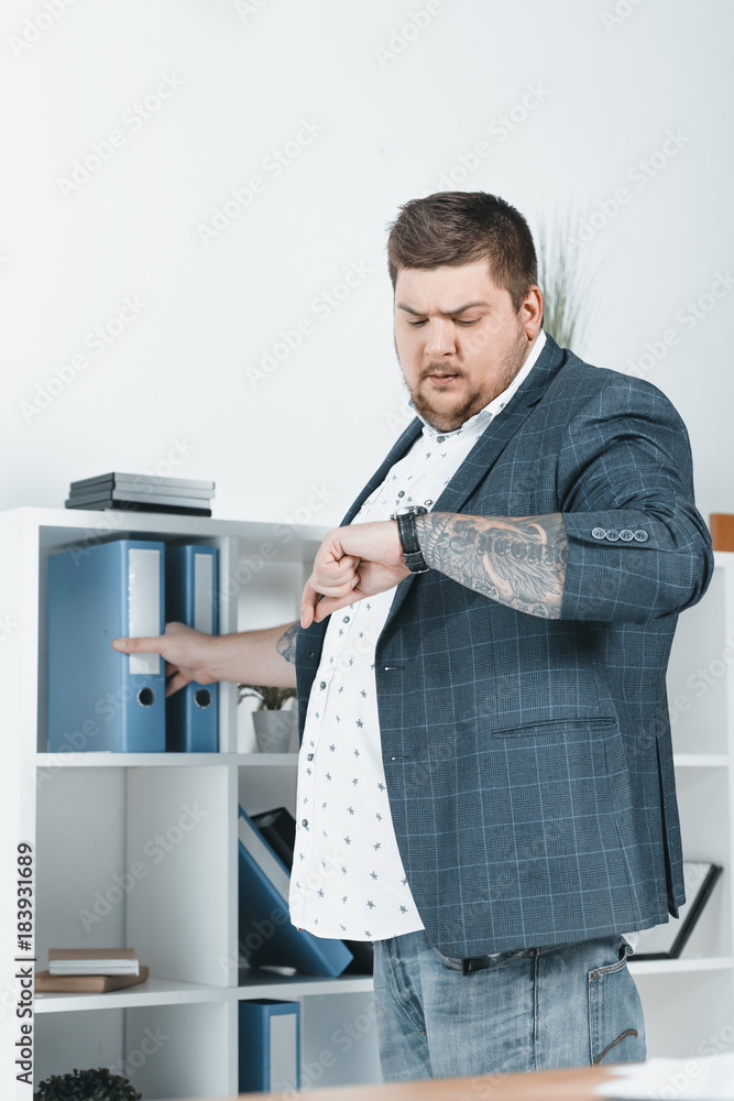 overweight businessman looking at watch while taking folders with ...