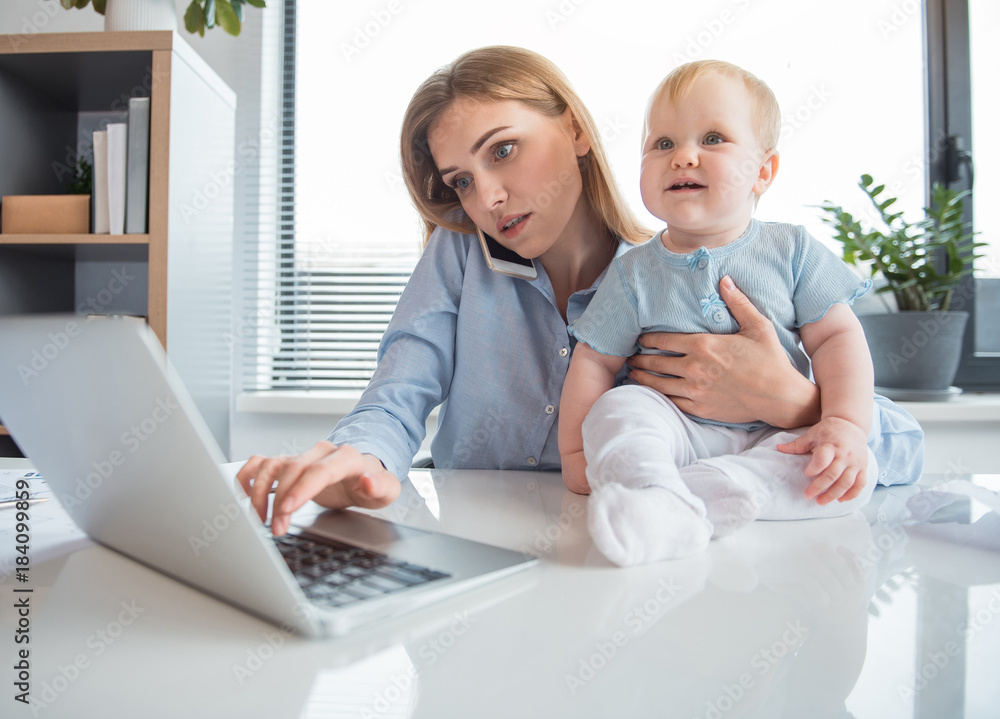 Portrait of serene mother typing in laptop and speaking by phone while ...