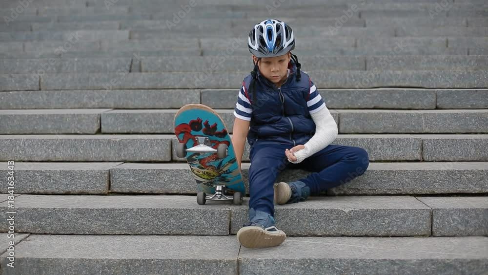 Bored white boy with broken arm sitting on the granite stairs and try ...