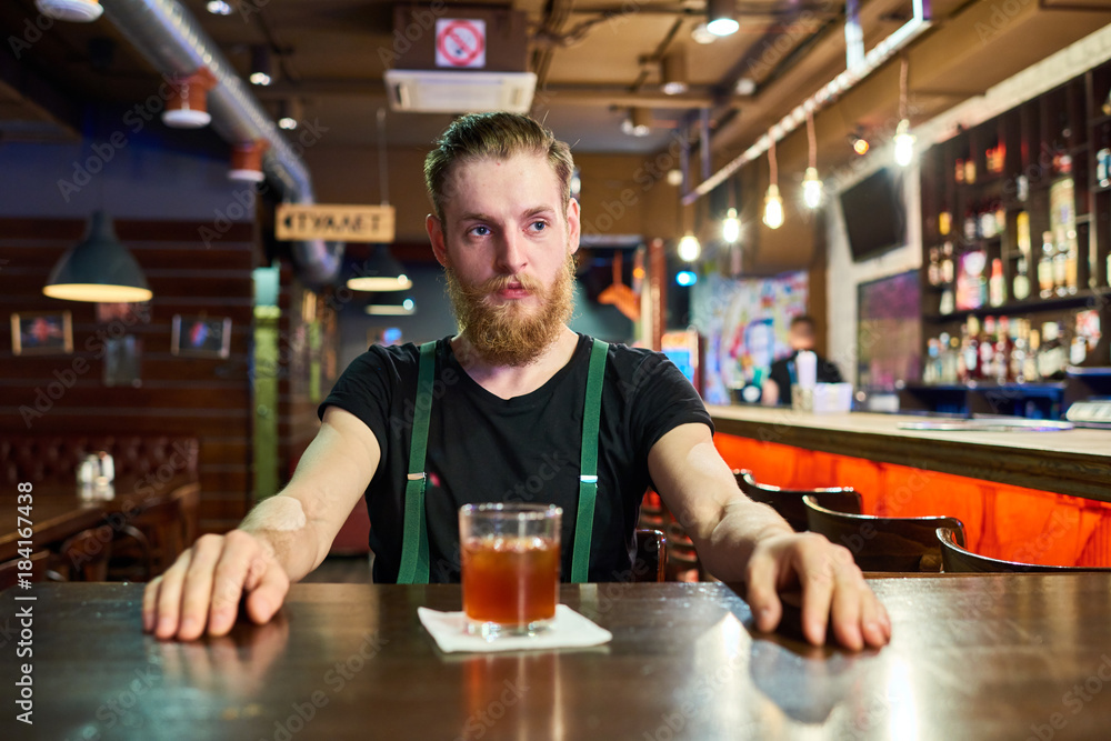 Portrait of modern bearded man getting drunk in pub sitting at table ...