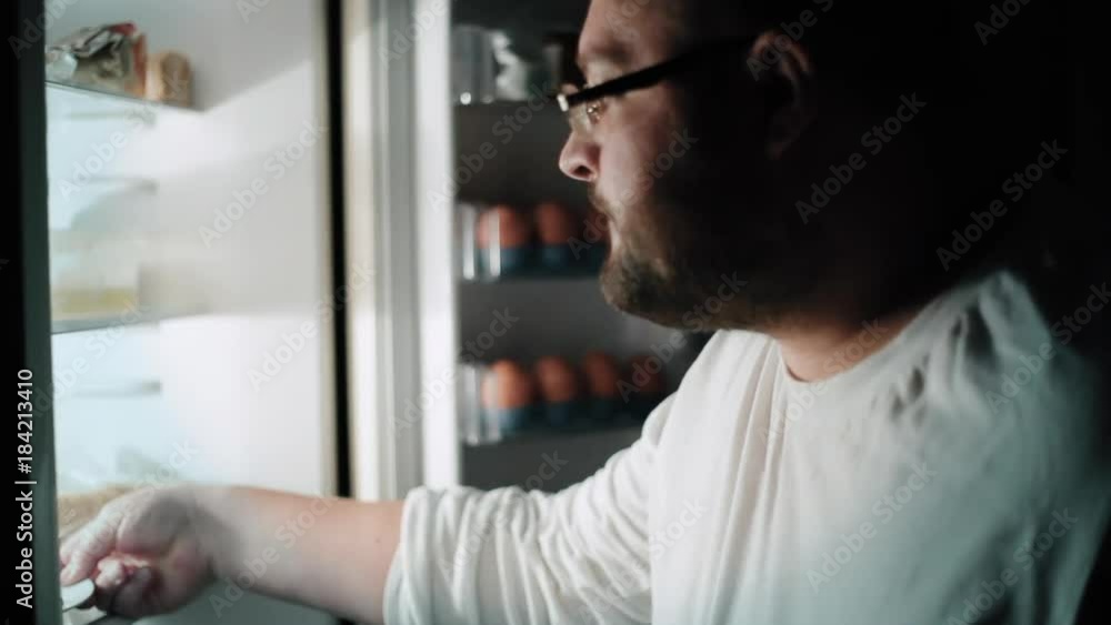 Fat man opens a refrigerator at night and eats a piece of cake, night ...