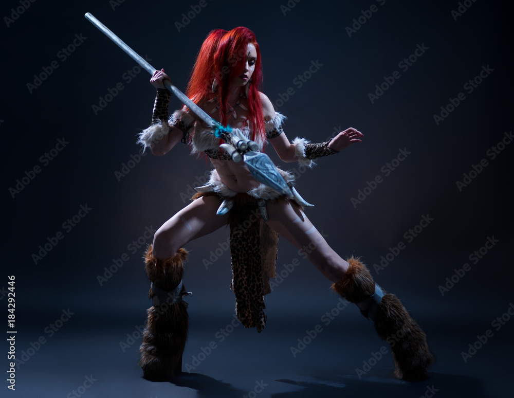 Beautiful red haired woman in stone age clothing with spear posing at ...