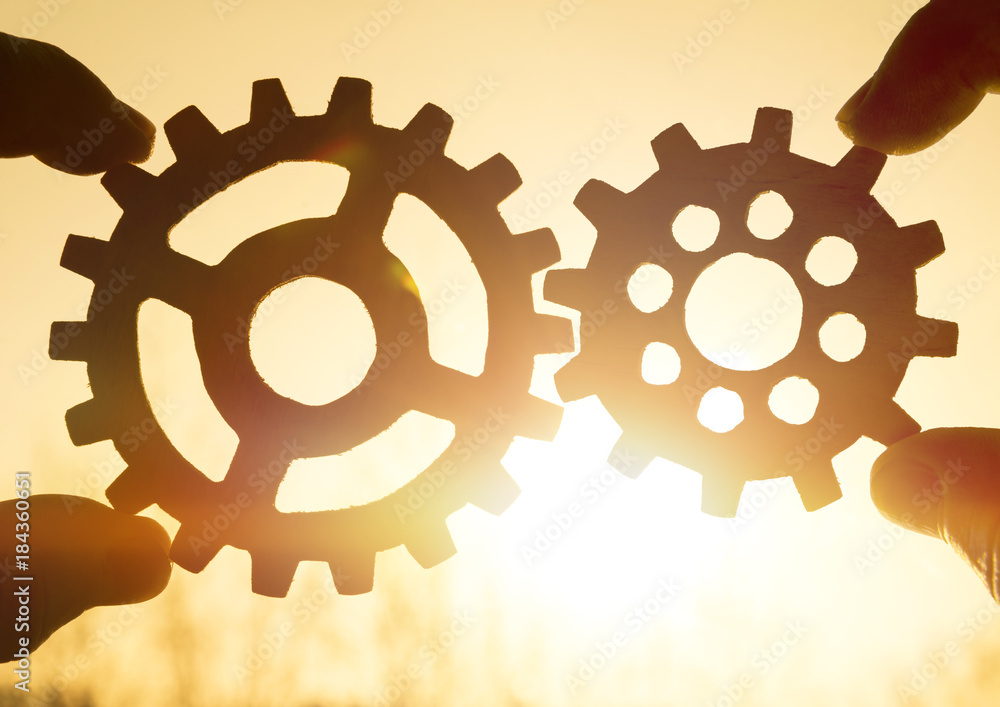 Two hands holding gears together. puzzle details on a sunset background ...