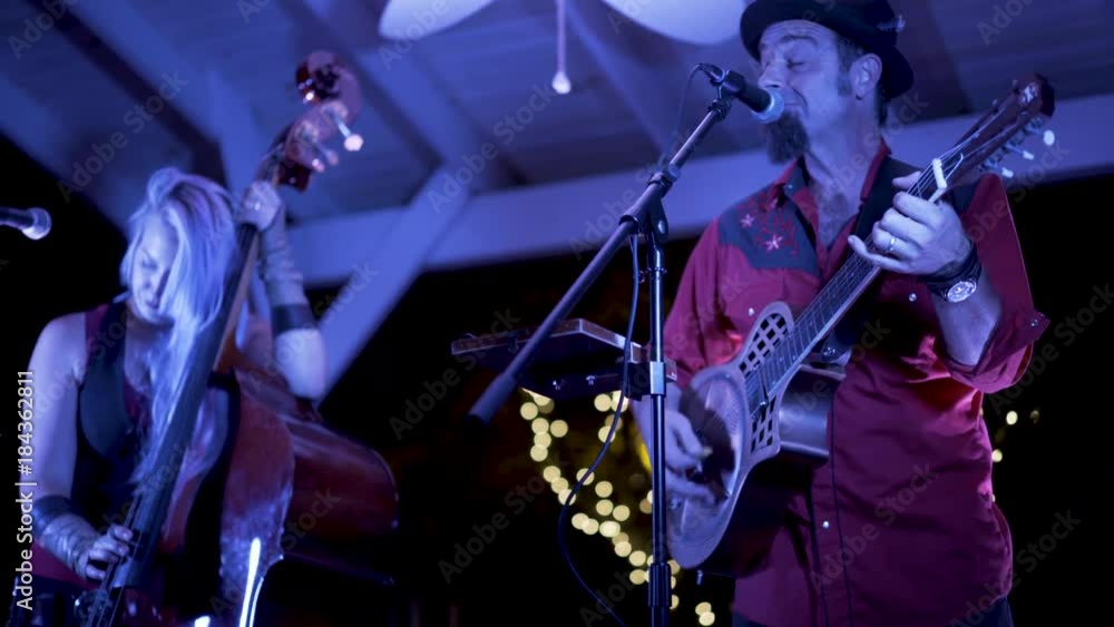 Resonator guitarist plays and sings into a microphone while a female ...