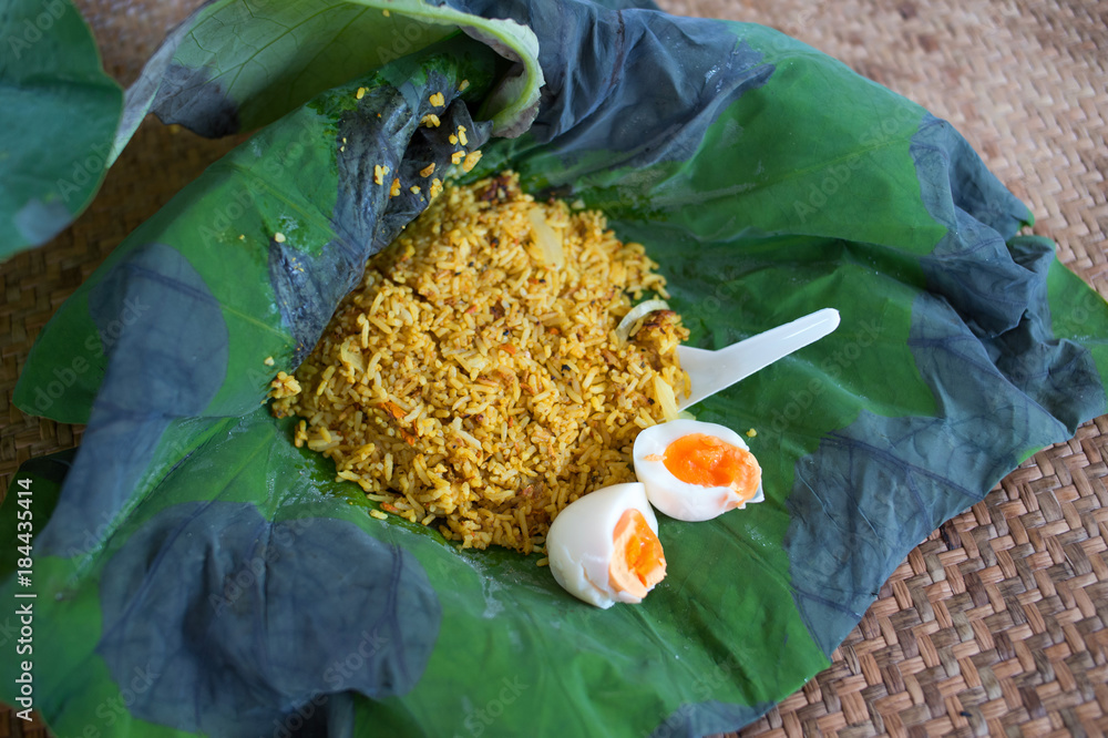 Fried rice mixed with turmeric on lotus leaves on top with piece of egg ...