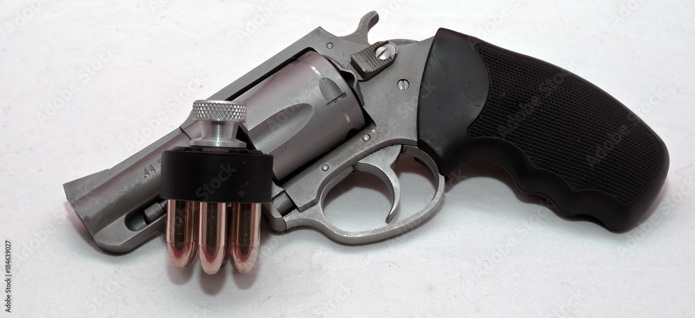 A stainless 44spl revolver with a loaded speed loader on a white ...