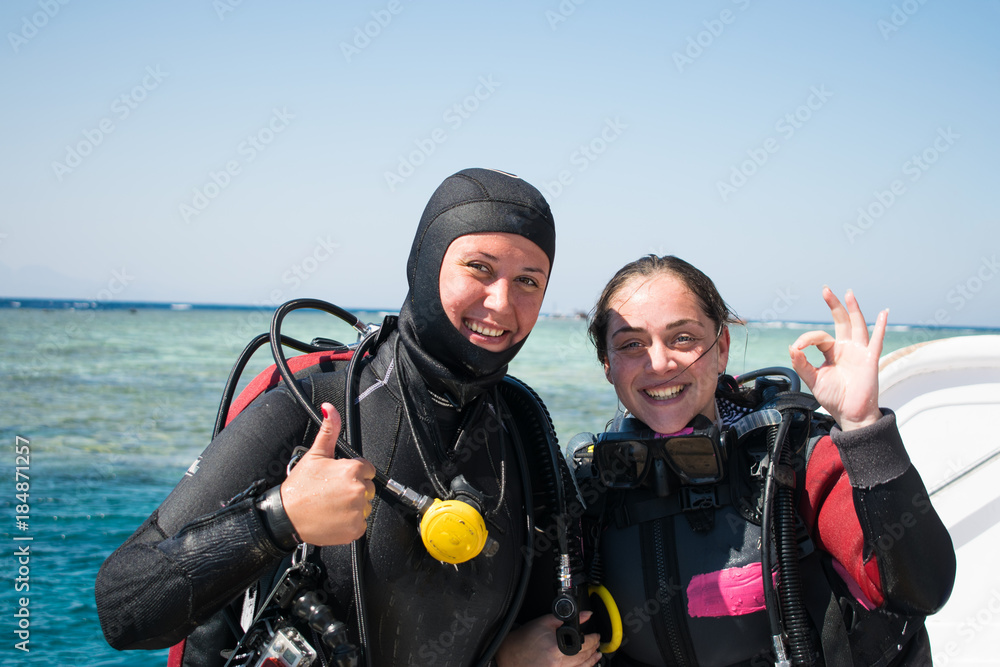 two smiling divers in wet suits show ok on the background of the sea ...