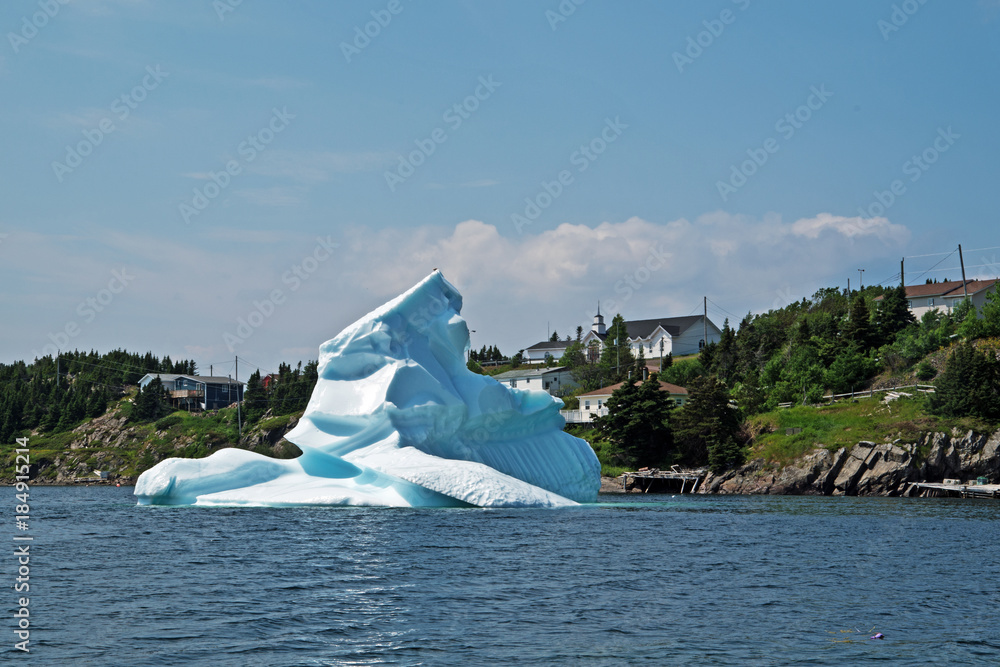 A mountain shaped iceberg grounded near shore in a coastal community ...