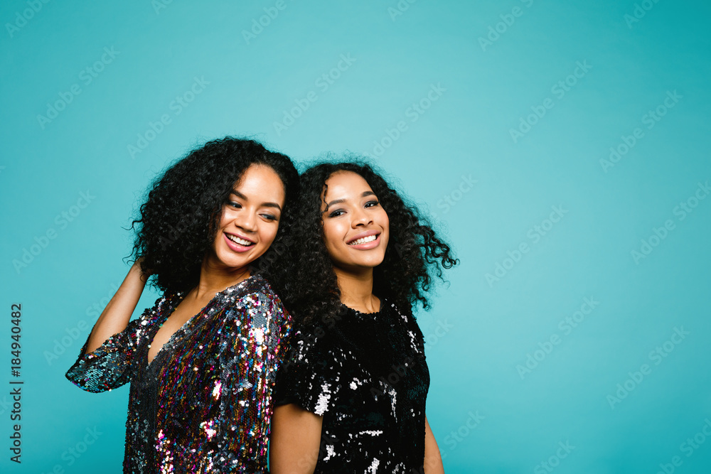 Portrait of a two mixed race women standing back to back against blue ...