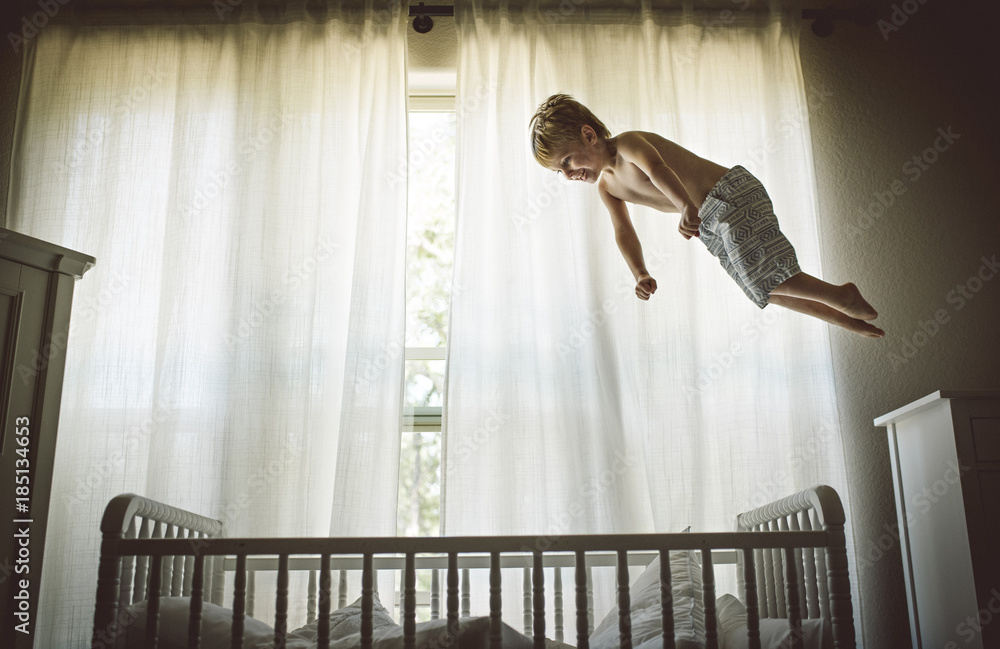 Shirtless boy levitating over crib against window at home Stock Photo ...