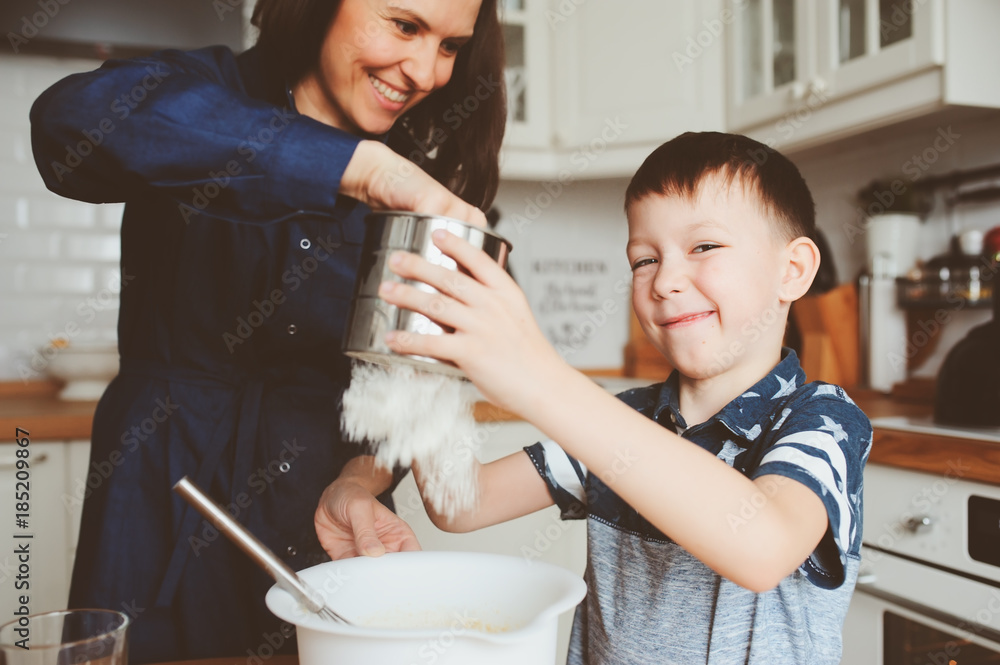 Kid boy helps mother to cook in modern white kitchen. Happy family in ...