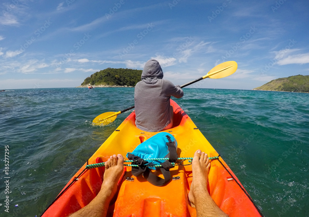 pair of young people are swimming on a kayak in the sea to the island ...
