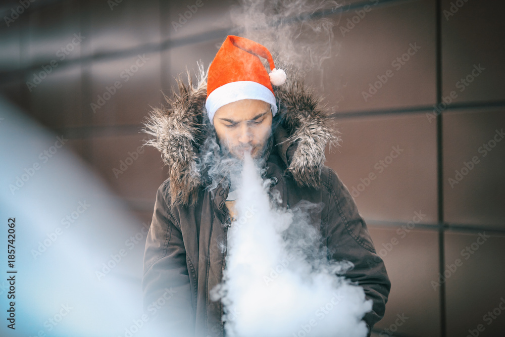 Vape man. Portrait of a handsome young white guy in a Santa Claus hat ...