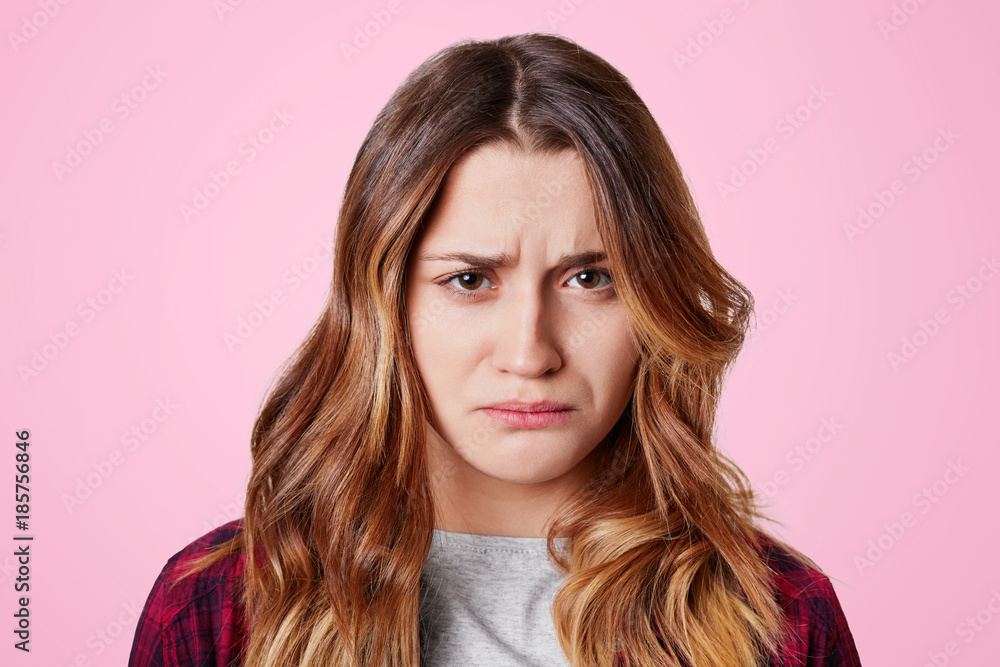 Headshot of unhappy sorrorful female curves lips, looks desperately at ...