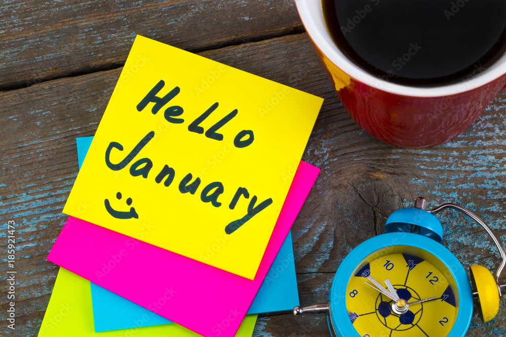 Hello January - handwriting in black ink on a sticky note with a cup of ...