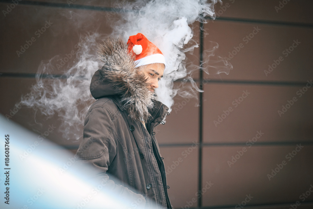 Vape man. Portrait of a handsome young white guy in a Santa Claus hat ...