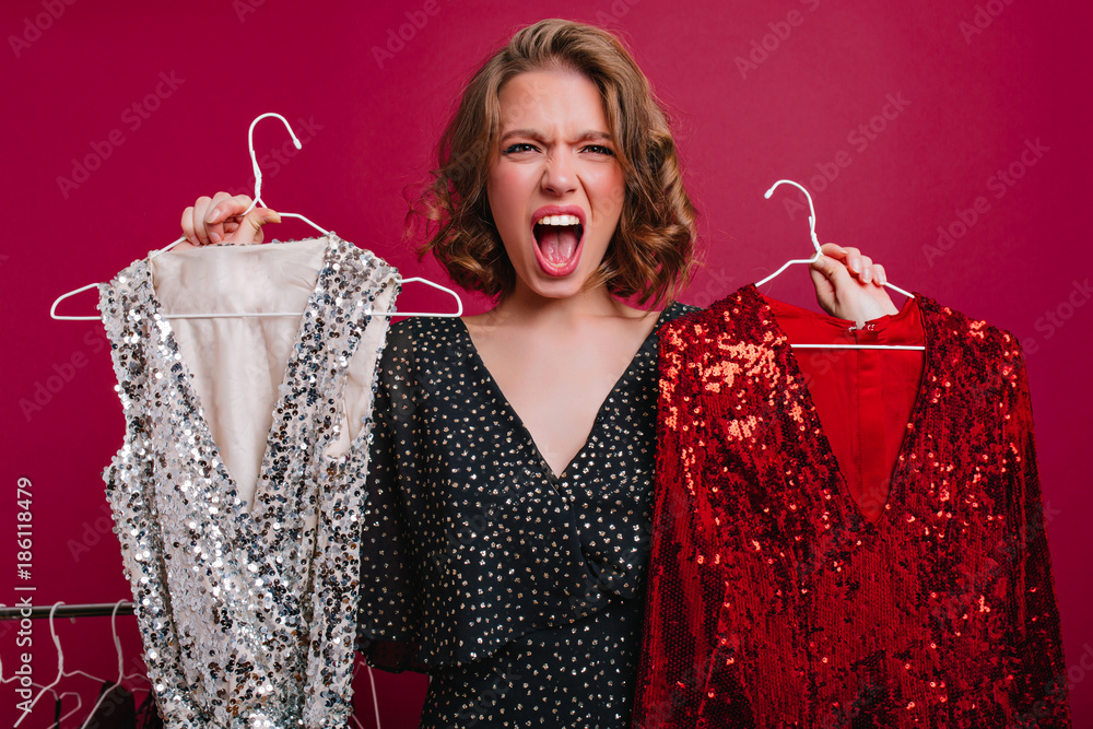 Close-up portrait of angry short-haired woman can't choose clothes for ...