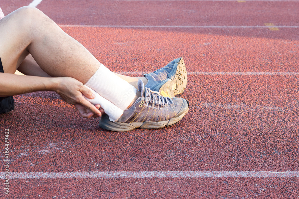 Male athlete applying compression bandage onto ankle injury of a ...